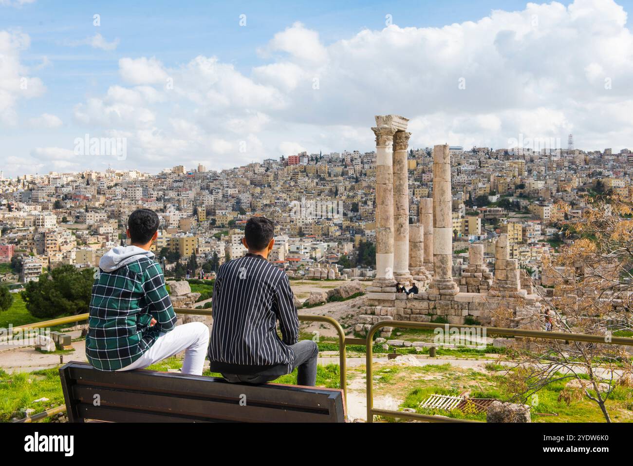 Two young Jordanian men sitting on a bench facing the Temple of ...