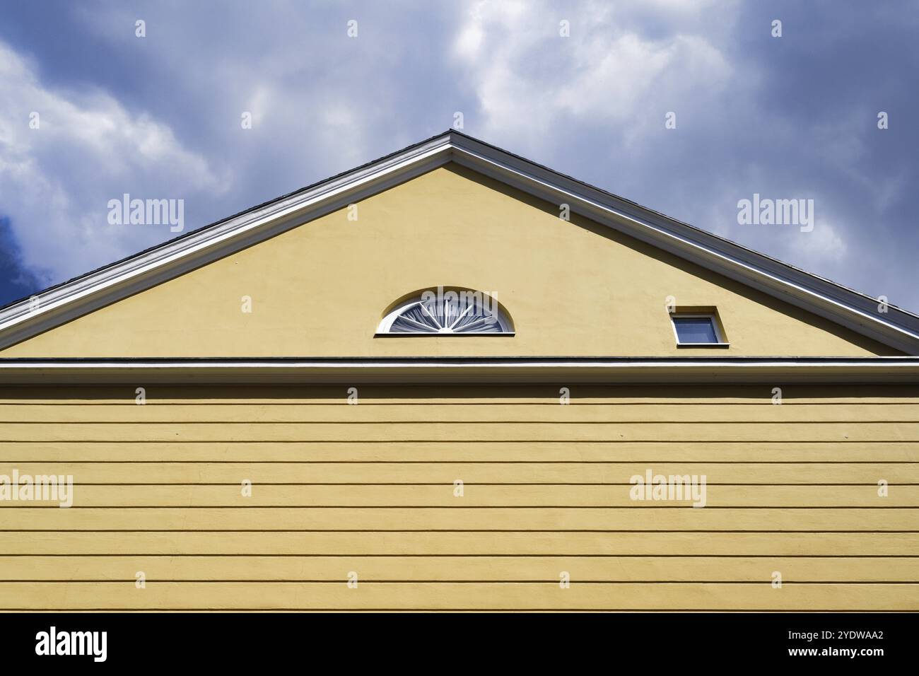 A yellow house with a pitched roof and one semi-circular and one square ...