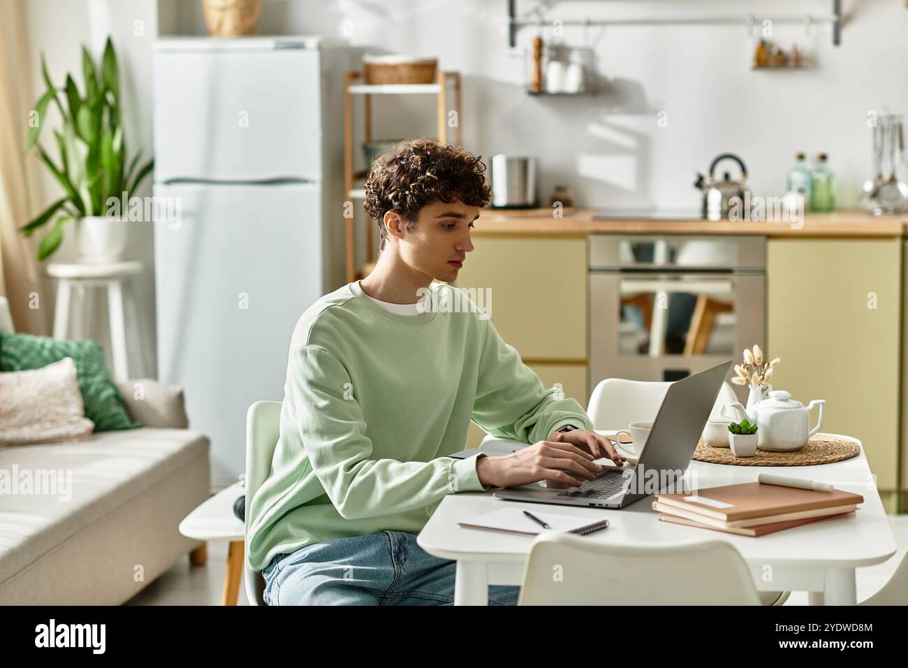 A focused young man types on his laptop at a stylish home office set up ...