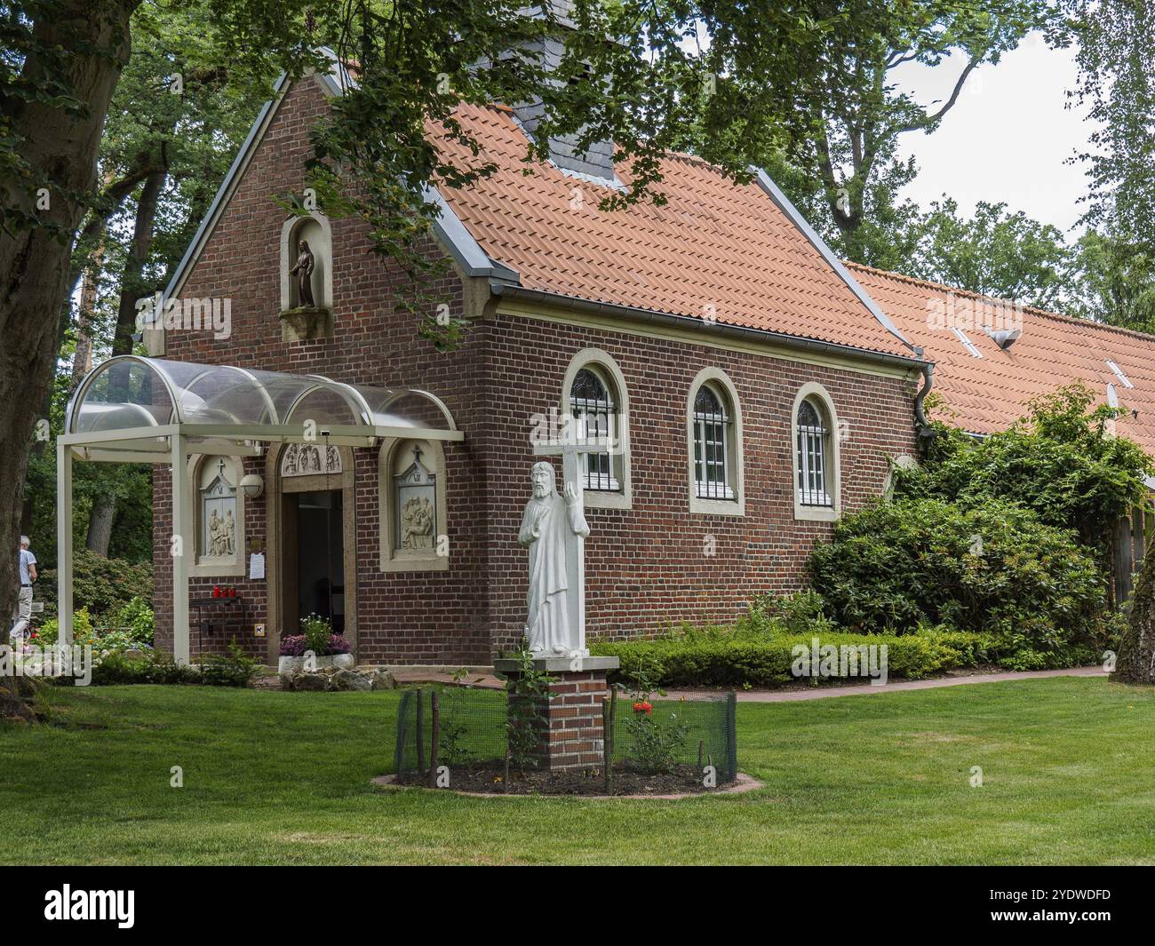 Small brick chapel with statue and well-kept garden surrounded by trees ...
