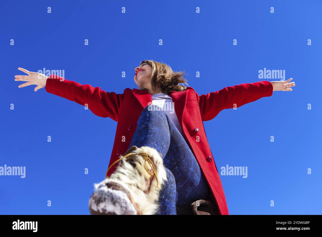 A happy Caucasian woman looks overjoyed with her arms raised against a ...