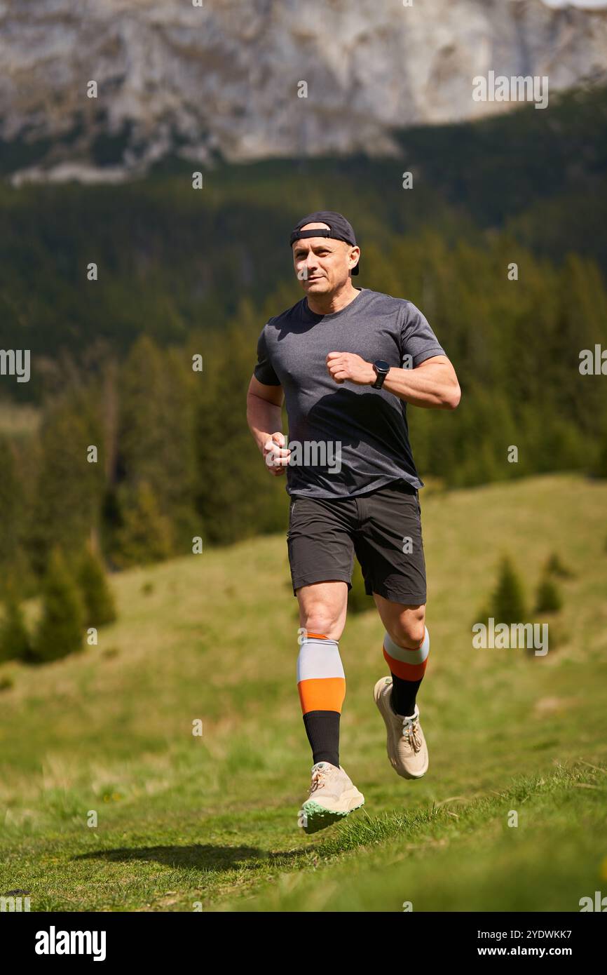 Trail runner man running on a meadow below the high mountain range ...