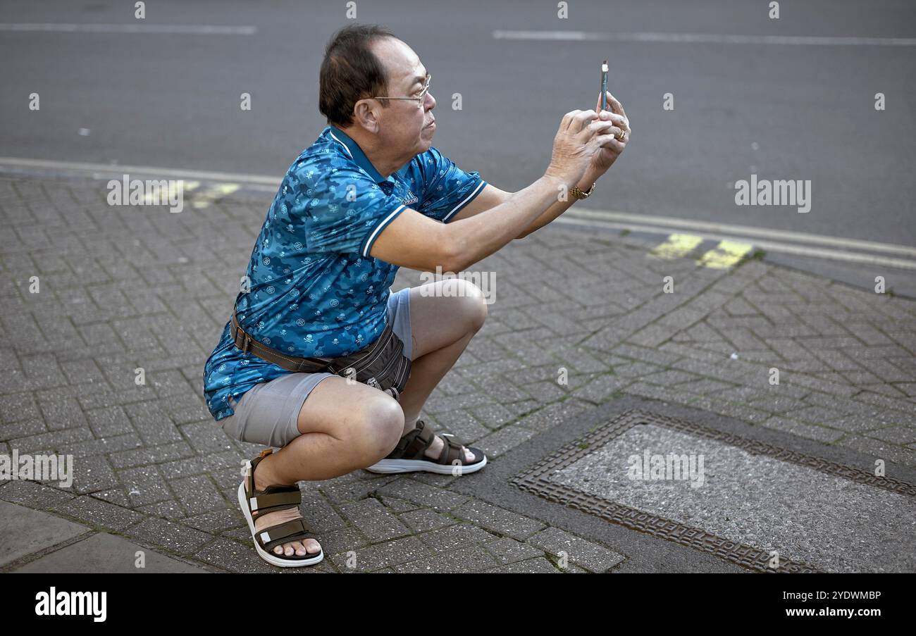 Chinese tourist crouching down to take a smartphone photograph. England ...