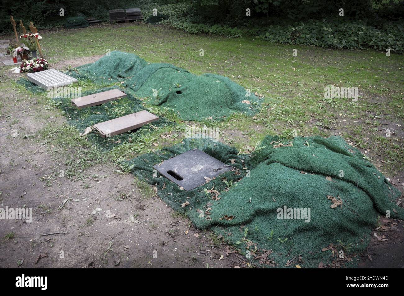 Several urn graves lined with green mats and fitted with protective ...