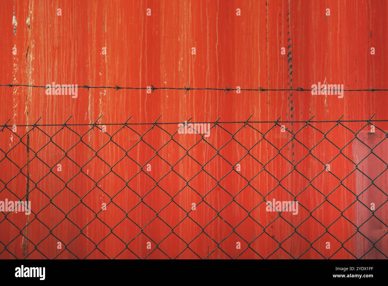 Old rusty worn chainlink fence against red metal container wall as ...