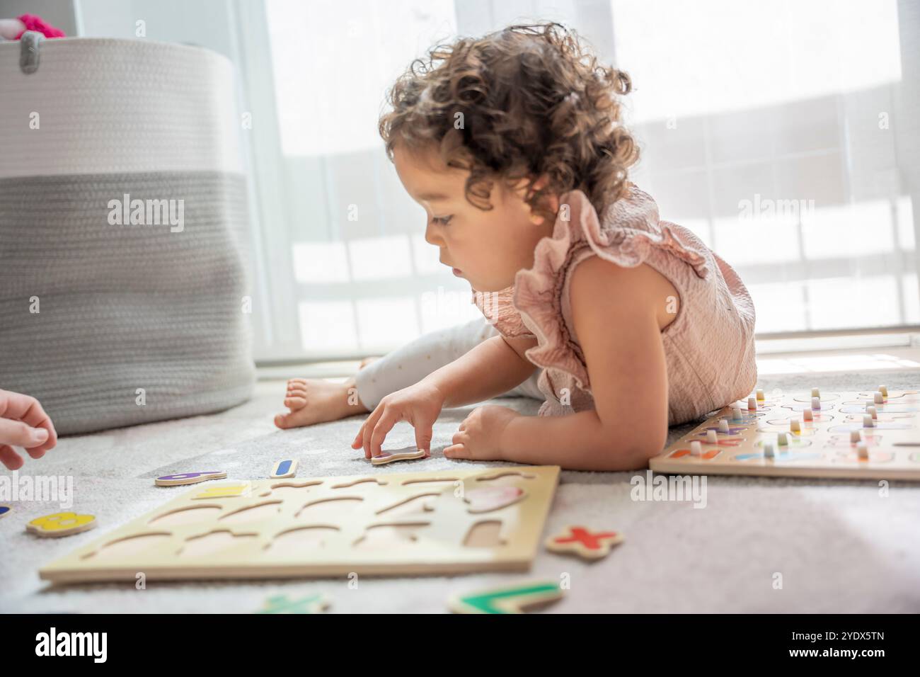 Close-up image of a little girl lying on a play mat playing with a wooden alphabet letter puzzle ...