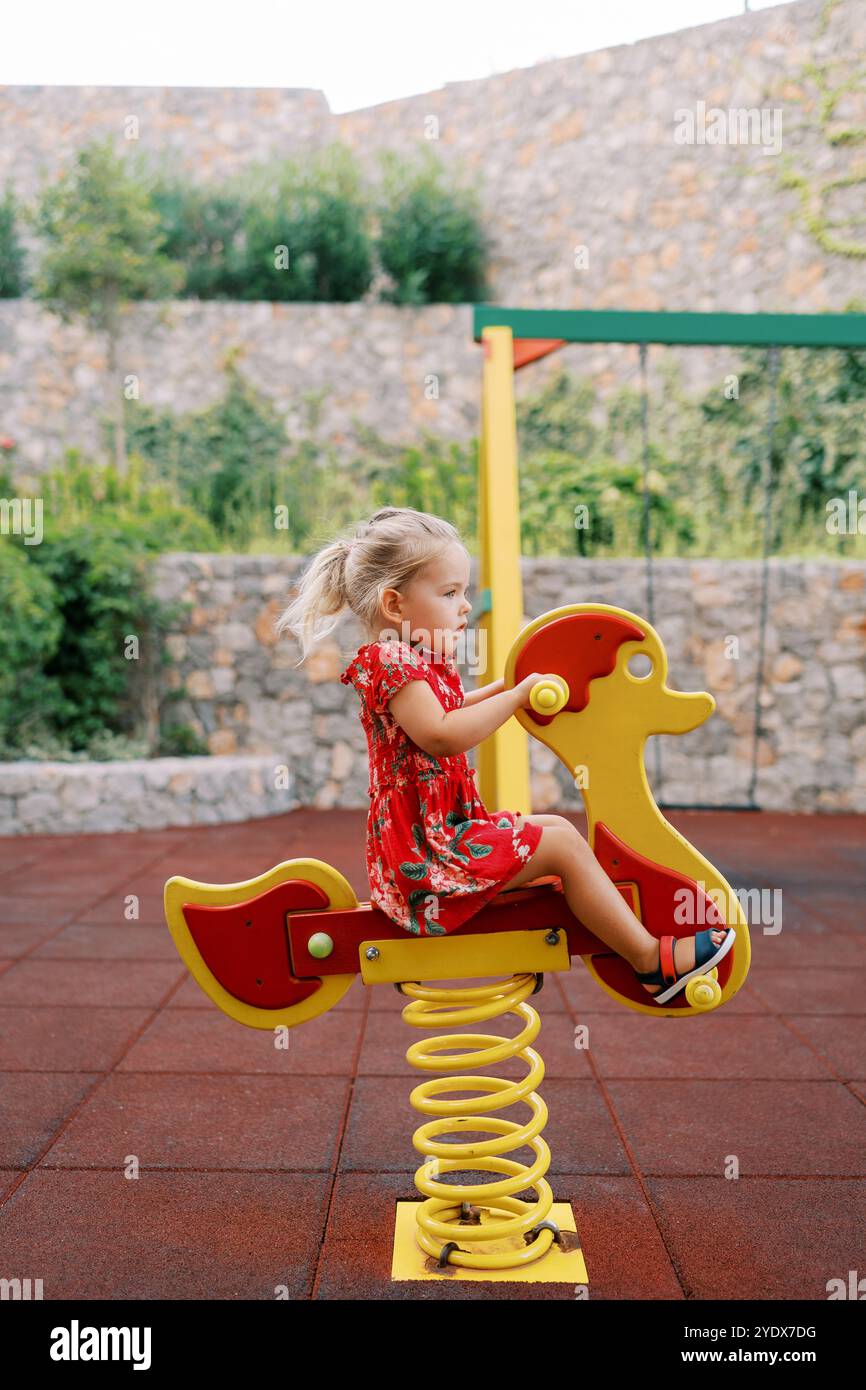 Little girl swings on a spring swing holding handles on the playground Stock Photo - Alamy