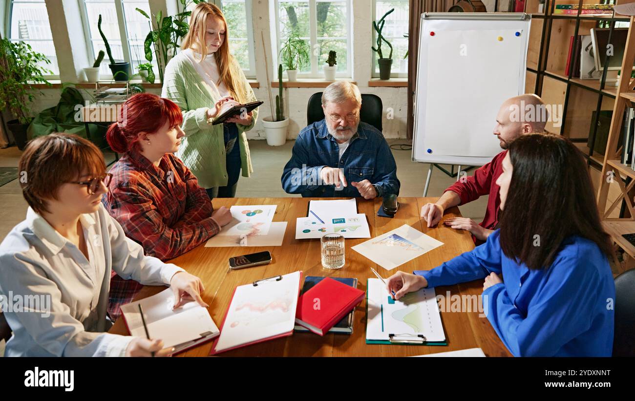 Group of business professionals engage in brainstorming session, surrounded by charts and graphs ...