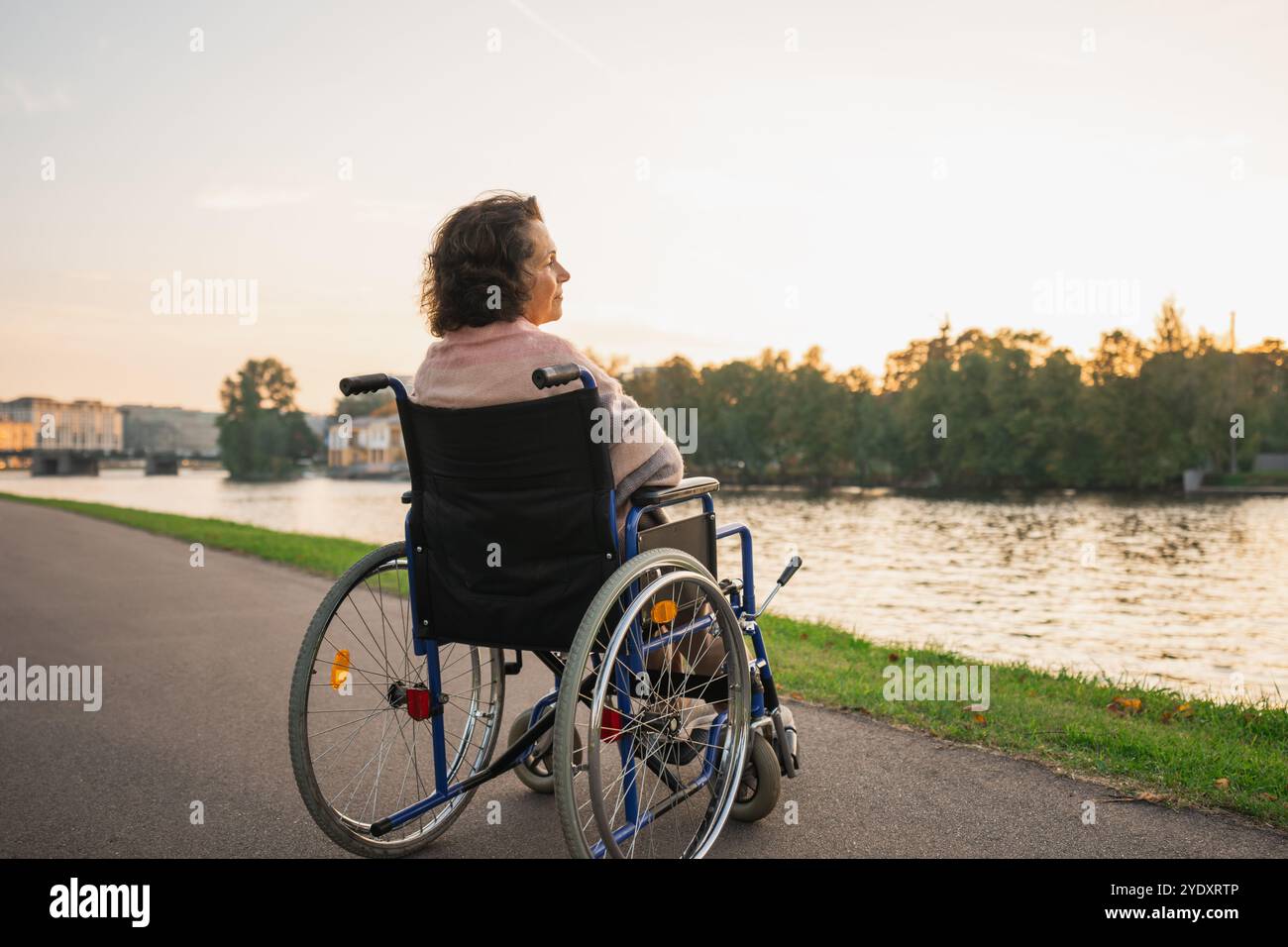 Sad senior woman sitting in wheelchair walking on road in city outdoor ...