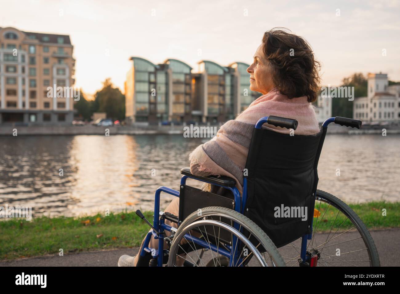 Sad senior woman sitting in wheelchair walking on road in city outdoor ...