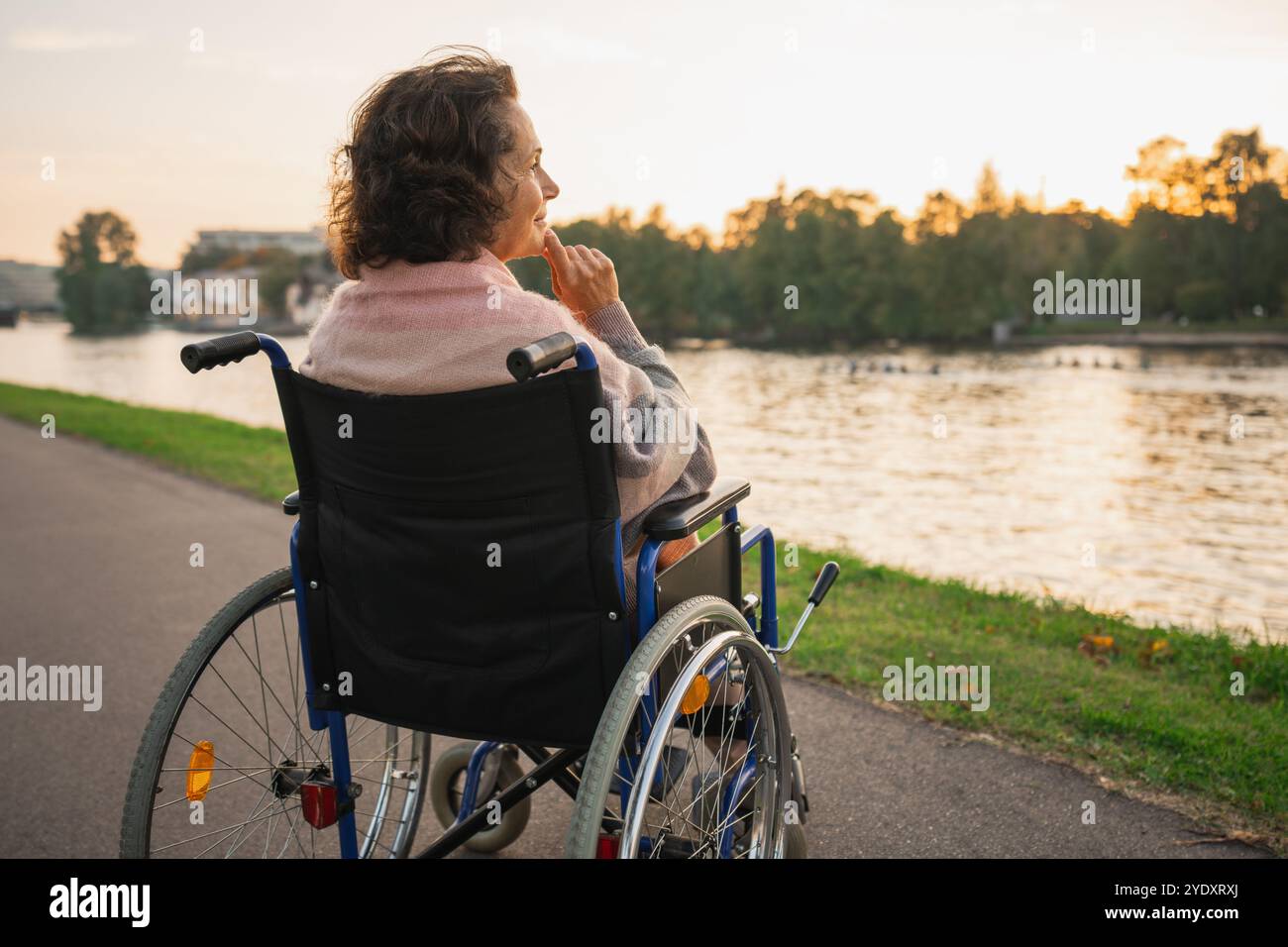 Sad senior woman sitting in wheelchair walking on road in city outdoor ...