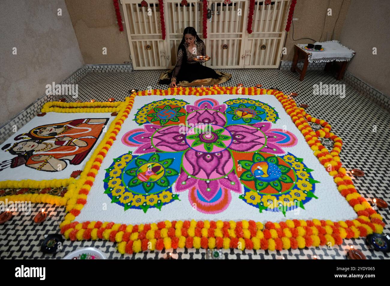 A girl places an earthen lamp beside a rangoli, a hand decorated ...