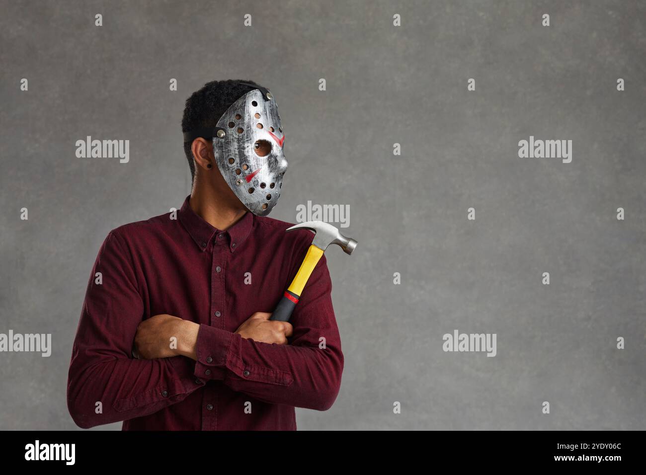 Black man in scary mask holding hammer and looking away on grey copy ...