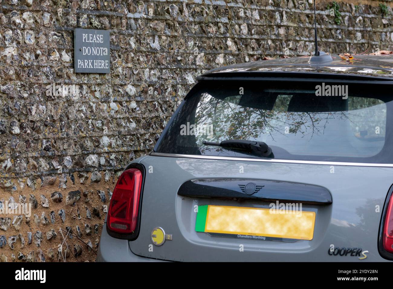 car parked by no parking sign on small village street stone brick wall ...