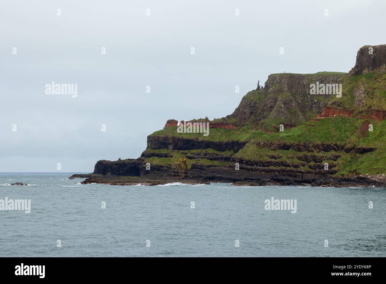 Layered cliffs with patches of green and reddish soil rise above the ...
