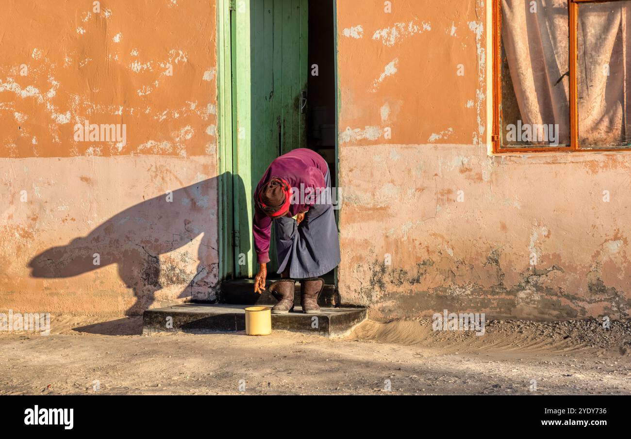 village african old woman standing in front of the house, picking a ...