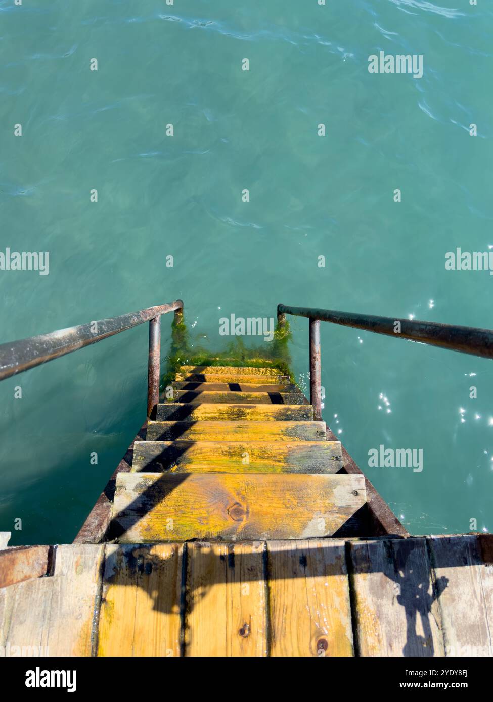 Yellow wooden steps with metal handrails descend into clear turquoise ...