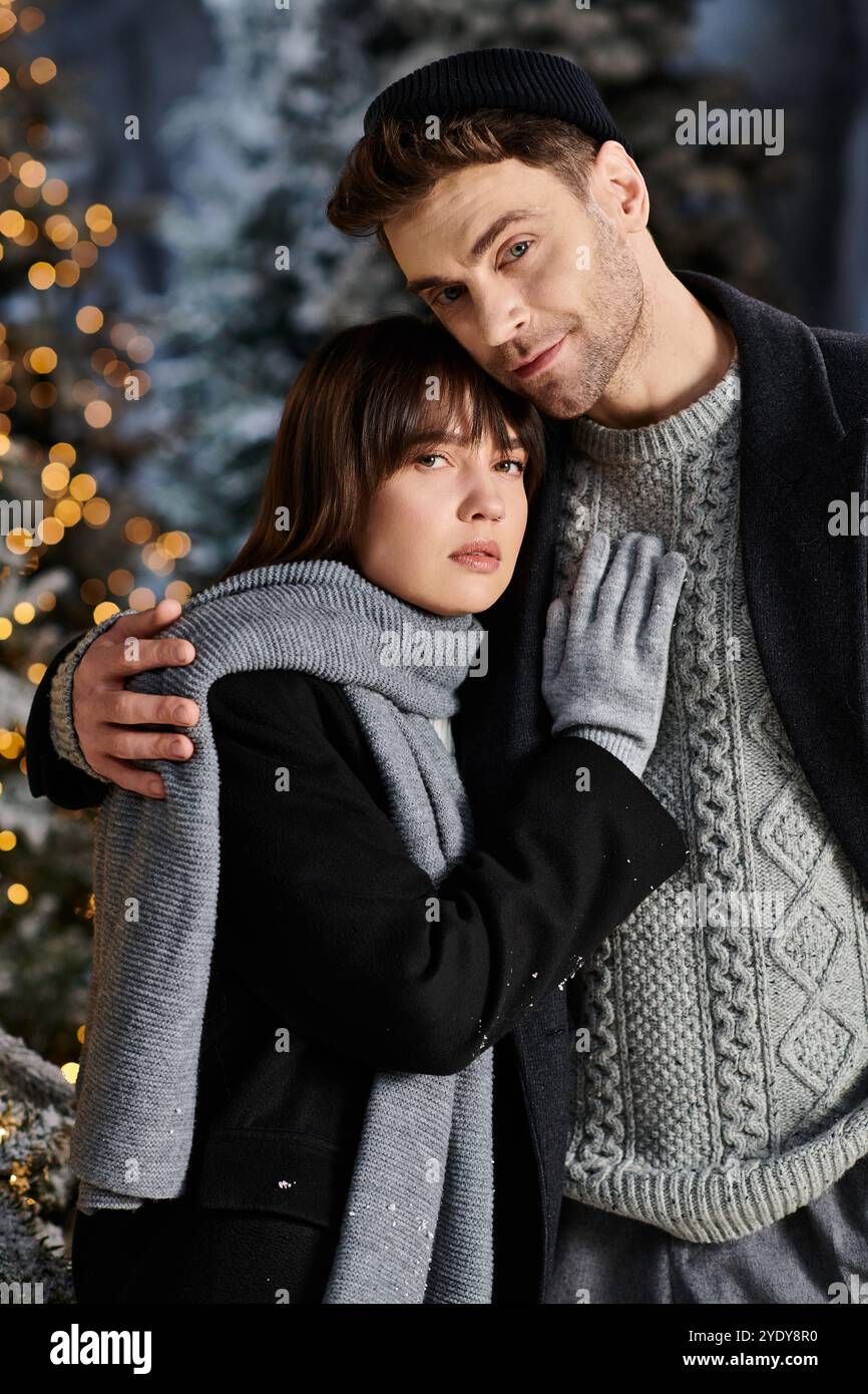 A couple in warm winter coats cuddles affectionately by the snowy pine ...