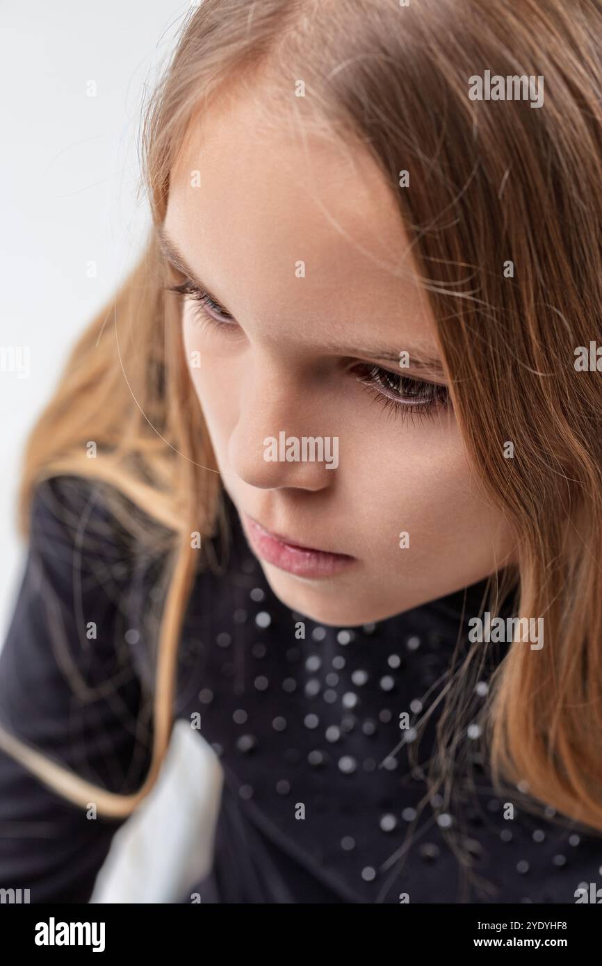 Pensive girl with long blond hair in dark shirt, looking down ...