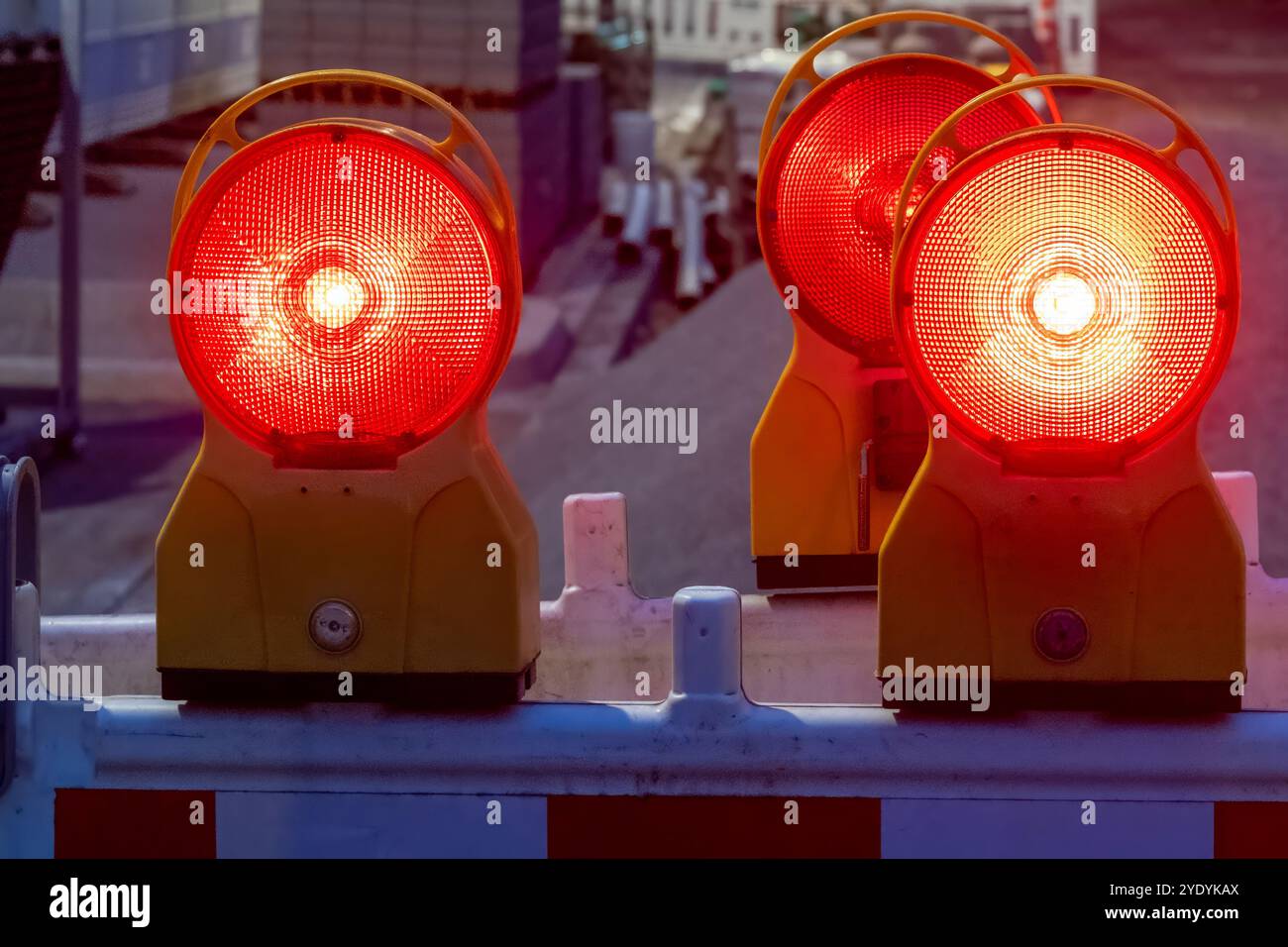 Red warning lights are flashing on a construction site barrier at dusk ...
