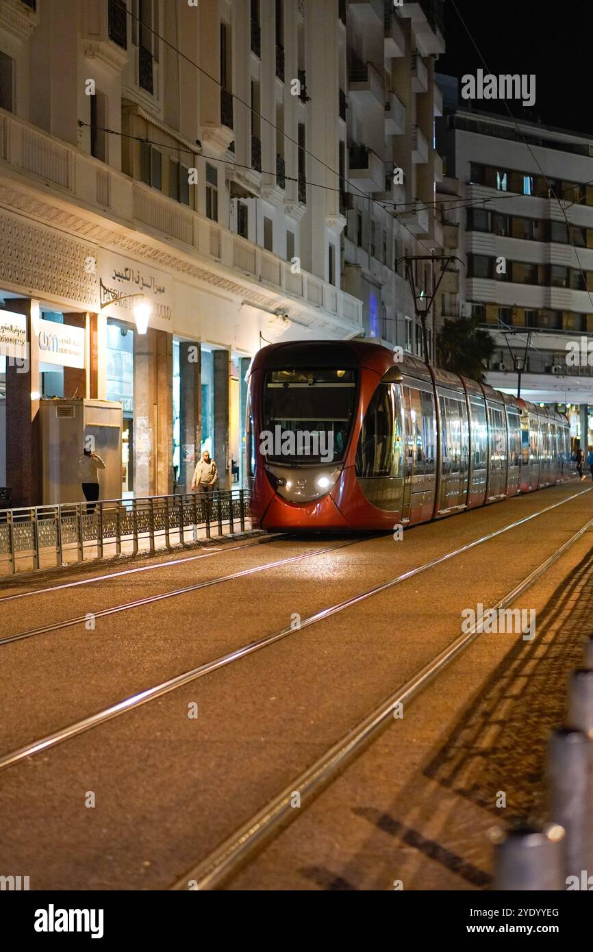 a red tram traveling on tracks through a city street at night, with ...