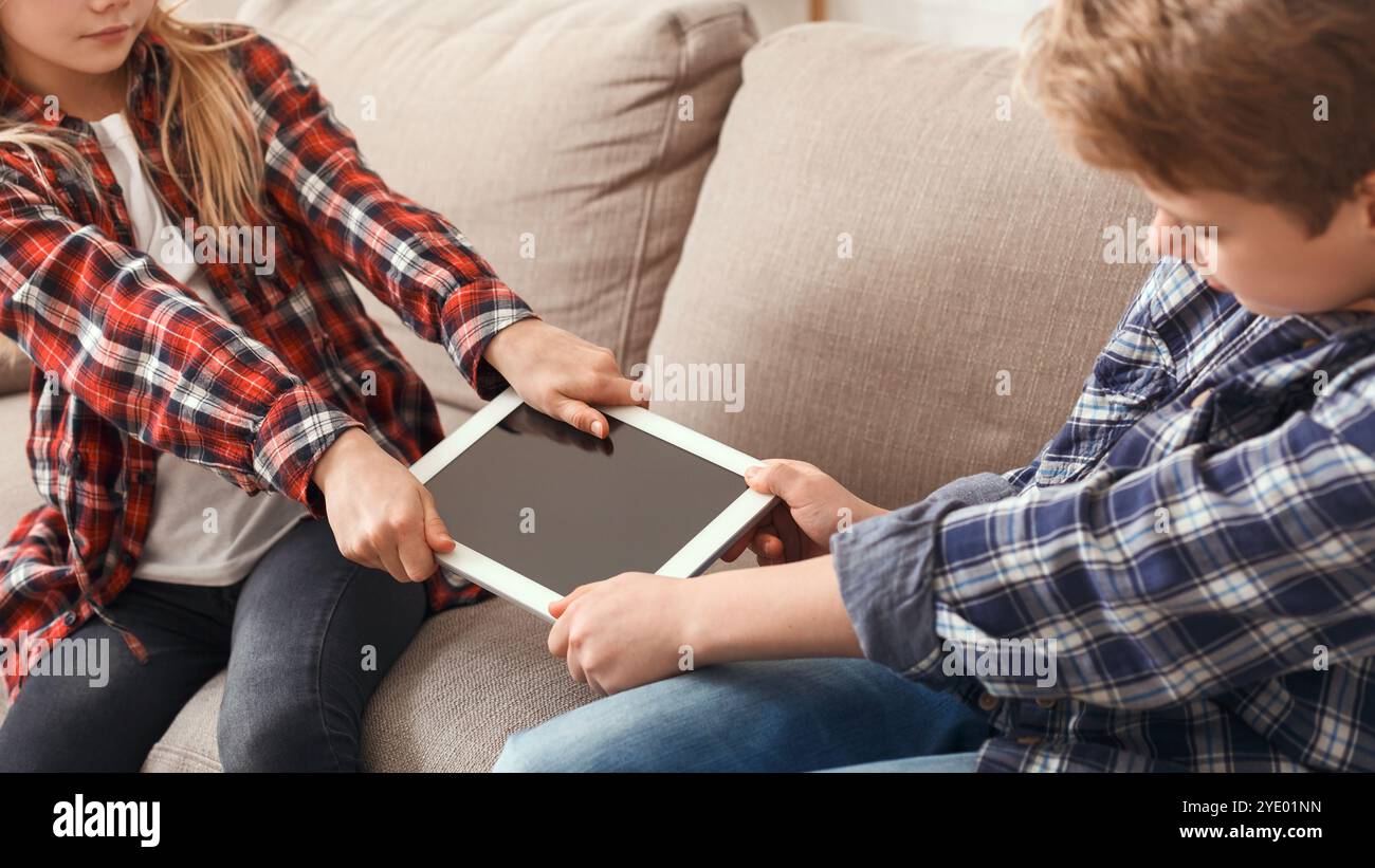 Jealous Brother And Sister Pulling Apart Tablet Sitting On Sofa Stock ...