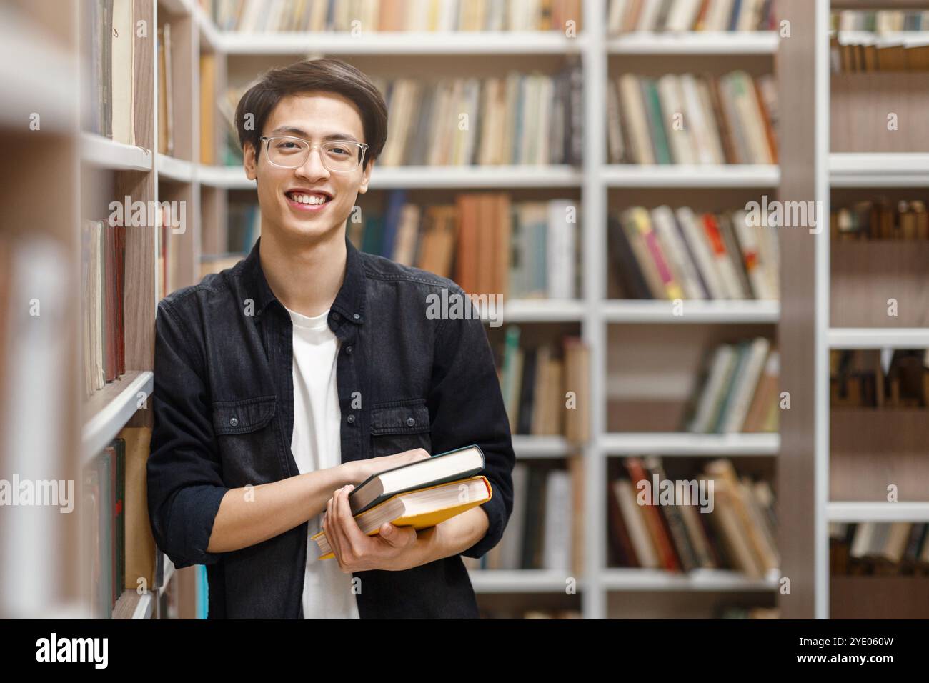 Smiling korean guy holding textbooks at library Stock Photo - Alamy