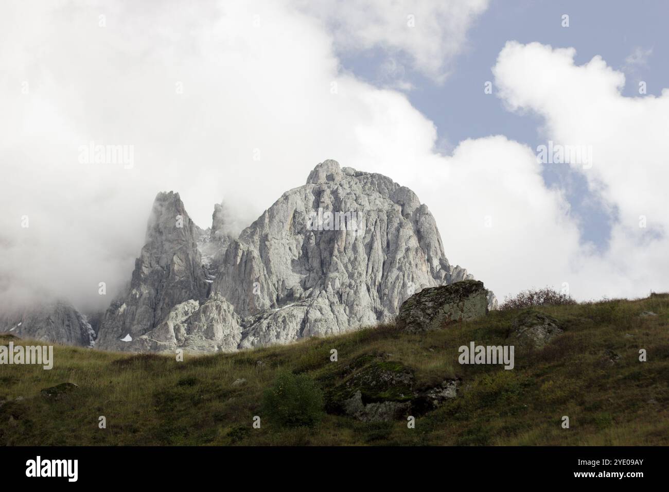 a towering, rugged mountain peak partly shrouded in clouds, adding a ...