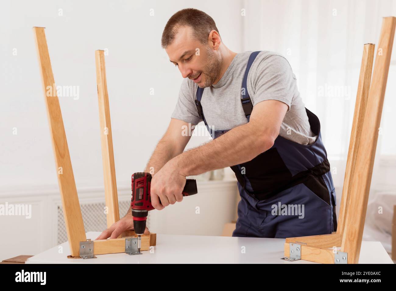 Repairman In Blue Uniform Fixing Table With Electric Drill Indoors ...