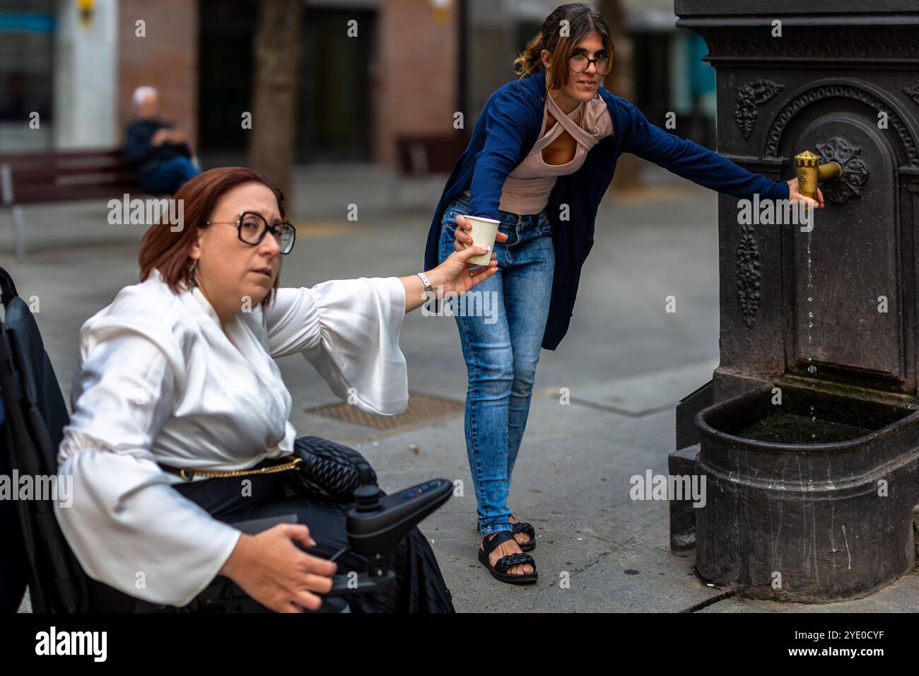 Wheelchair User Receiving Assistance at Public Fountain Stock Photo - Alamy