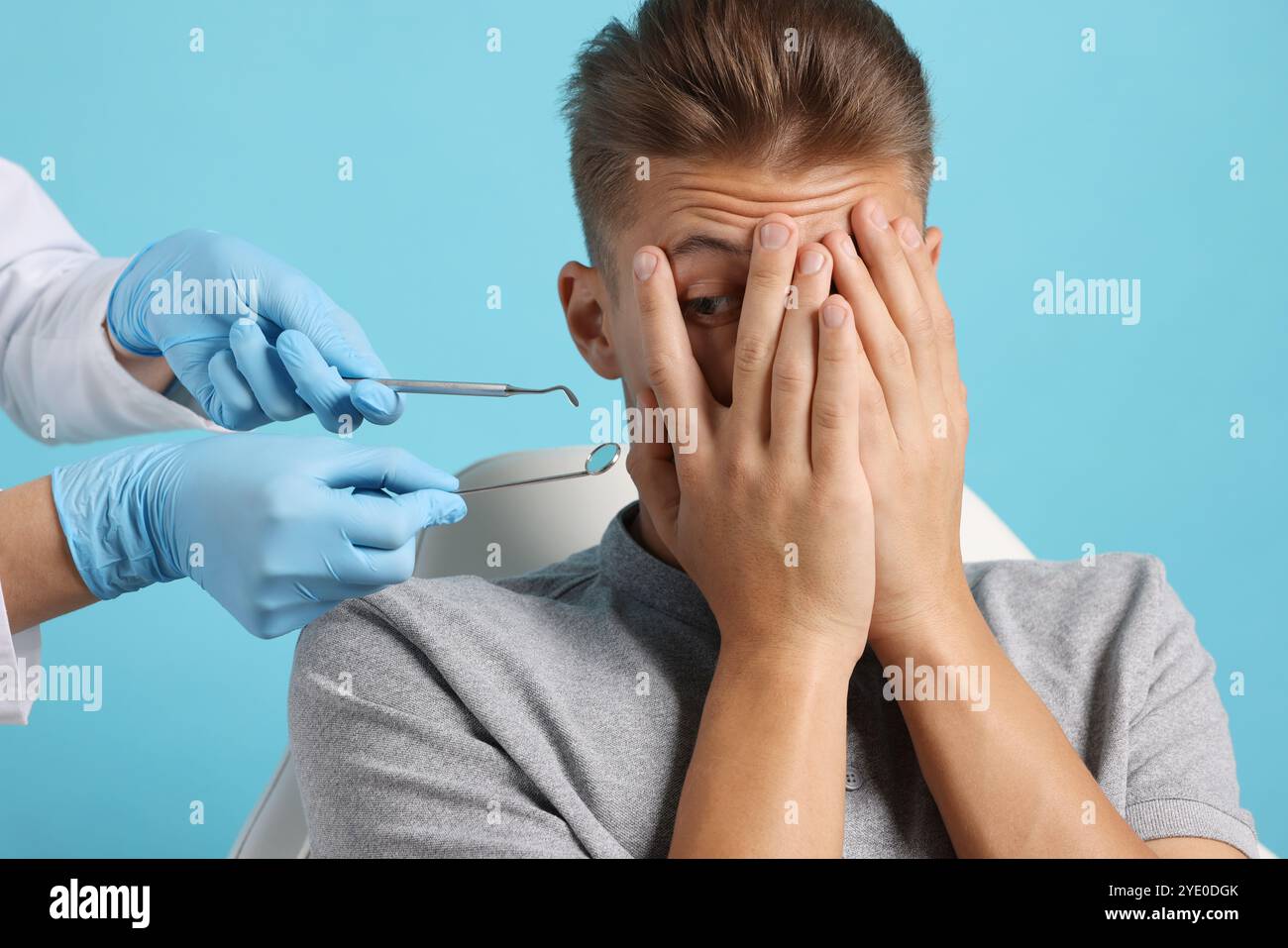 Dental phobia. Dentist working with scared man on light blue background ...