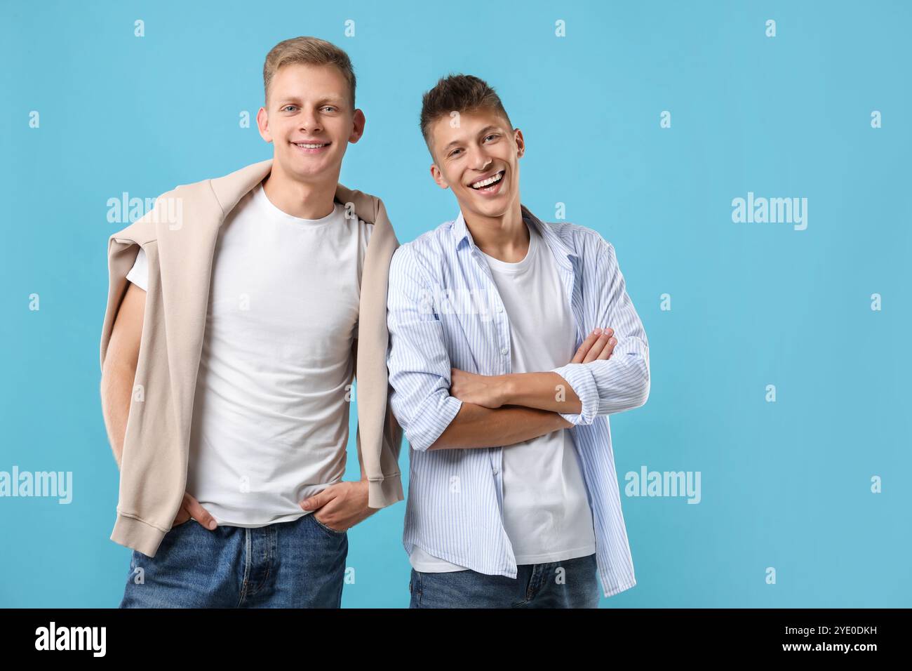 Young brothers posing with crossed arms on light blue background. Space ...