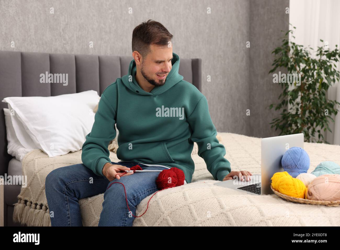 Man learning to knit with online course on bed at home Stock Photo - Alamy