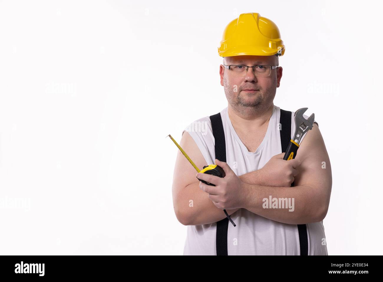 A construction worker wearing a yellow hard hat is holding tools and is ...