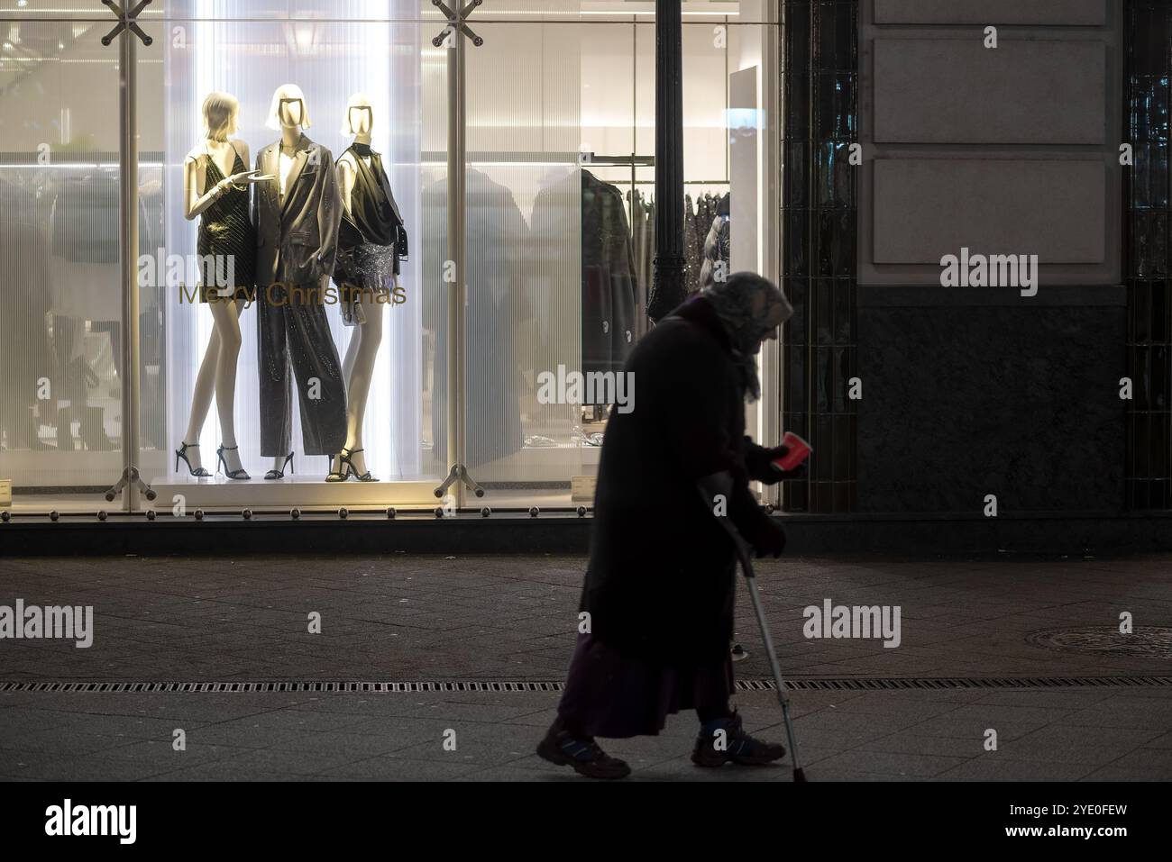 Old lady passing shop window holding paper cup for alms Stock Photo - Alamy
