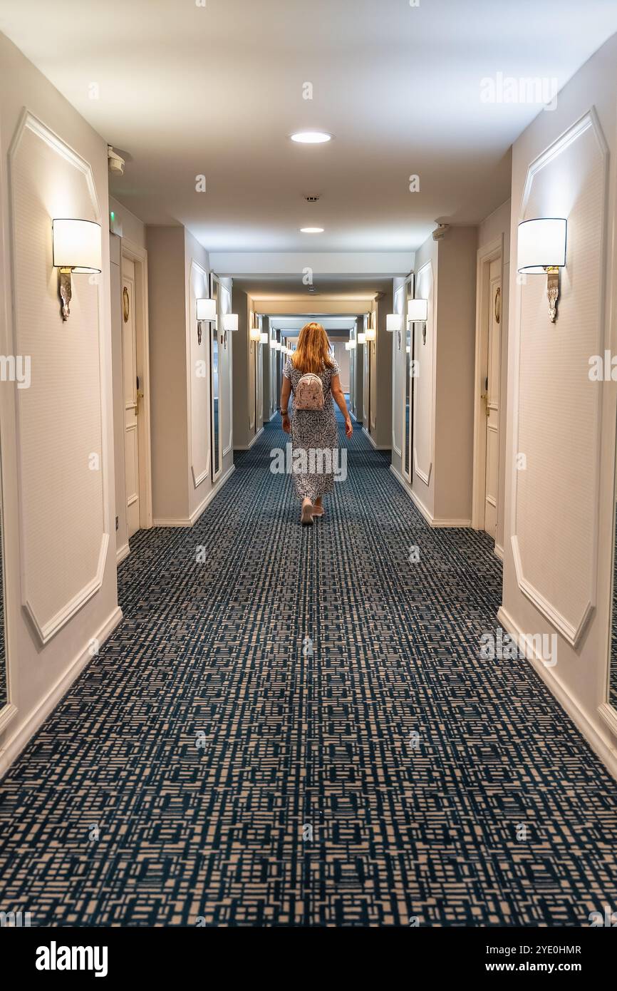 Female traveler from behind with backpack walking down a long corridor ...