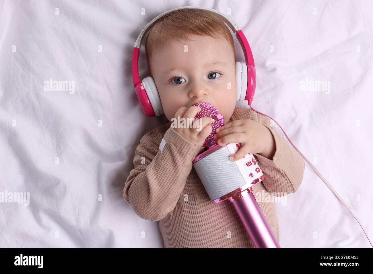 Cute little baby with headphones and microphone lying on bed, top view ...