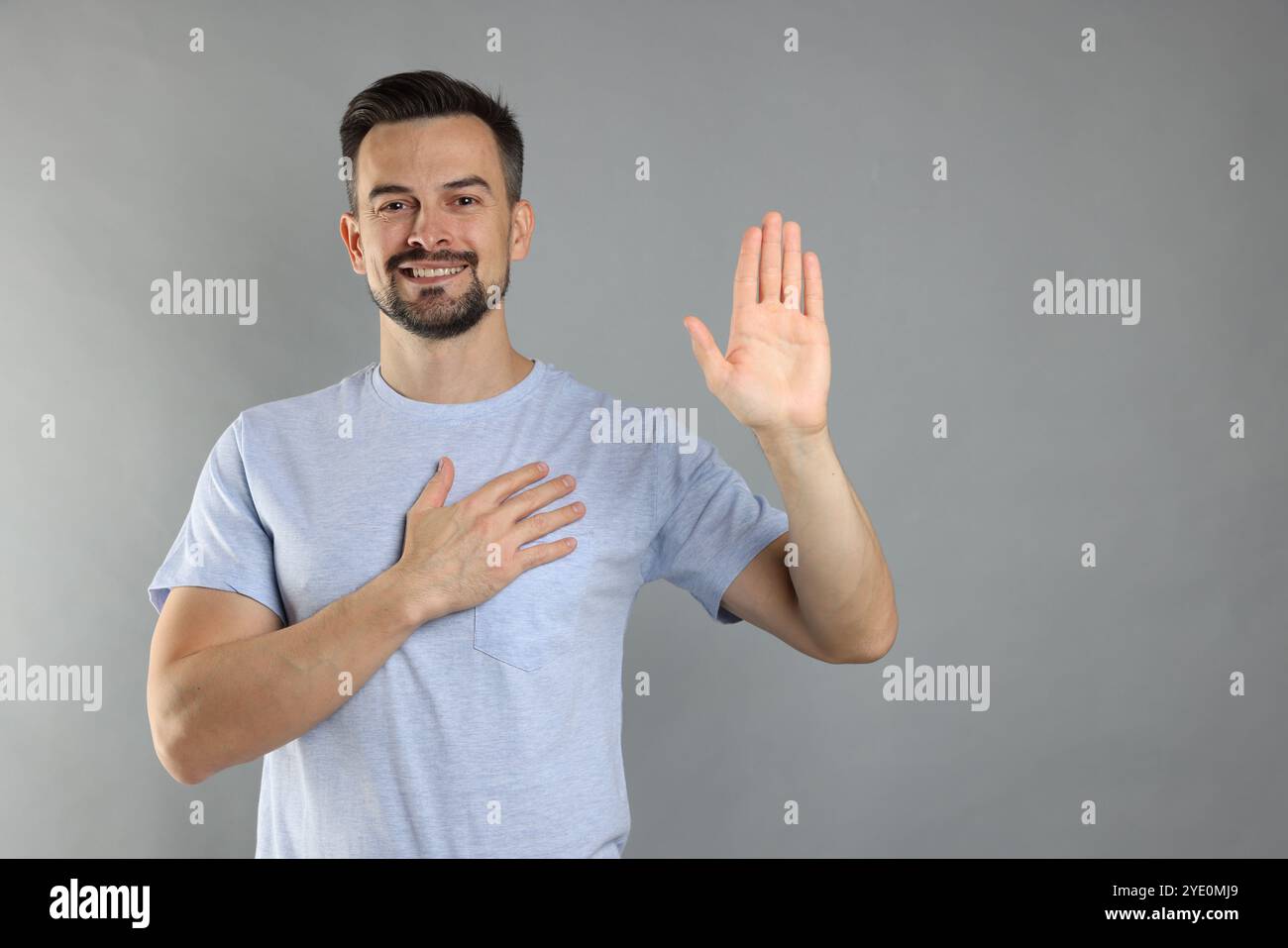 Man making promise with raised hand on grey background, space for text ...