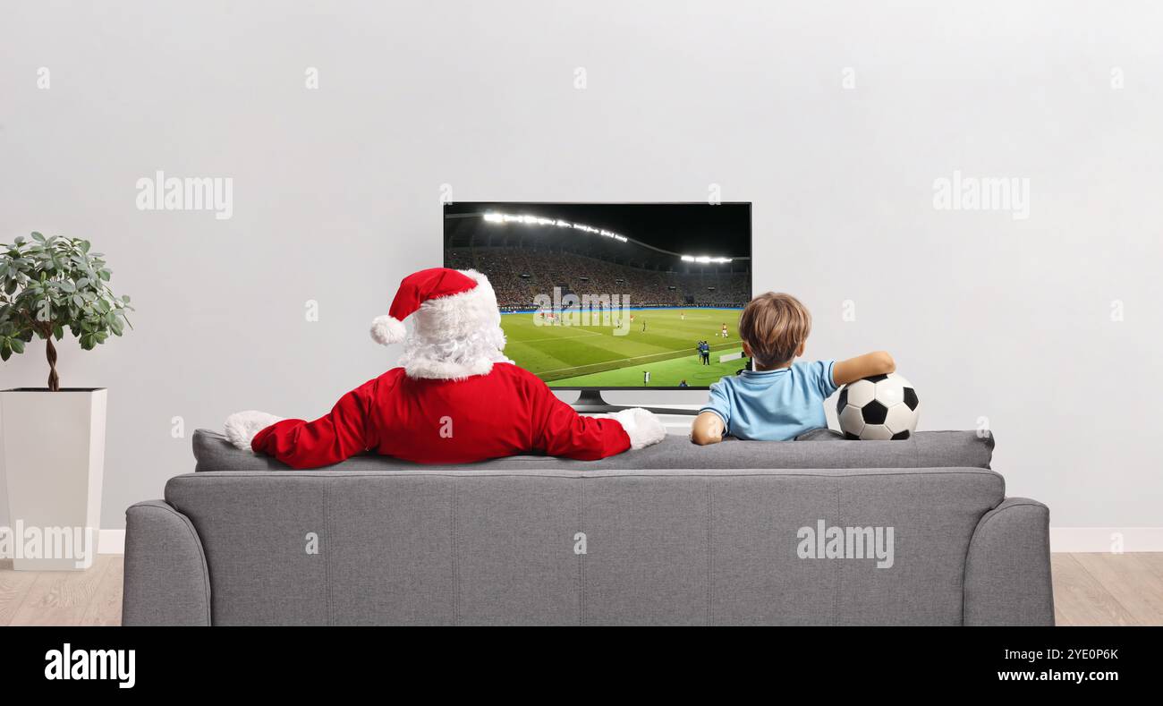 Santa claus watching a football match on tv at home with a kid seated ...