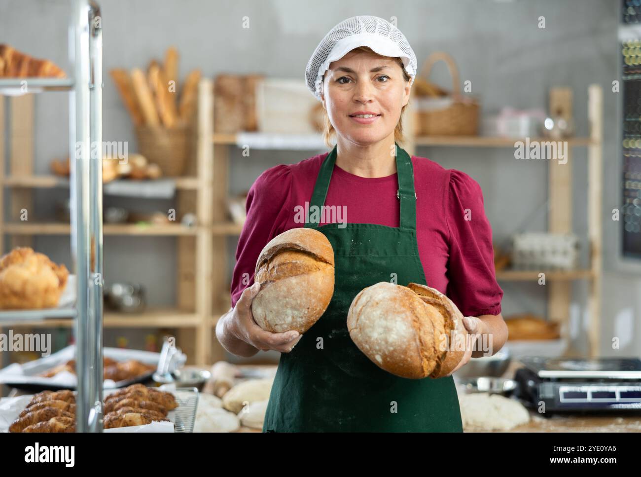 In working room of bakery, there is woman with loafs of bread in hands ...