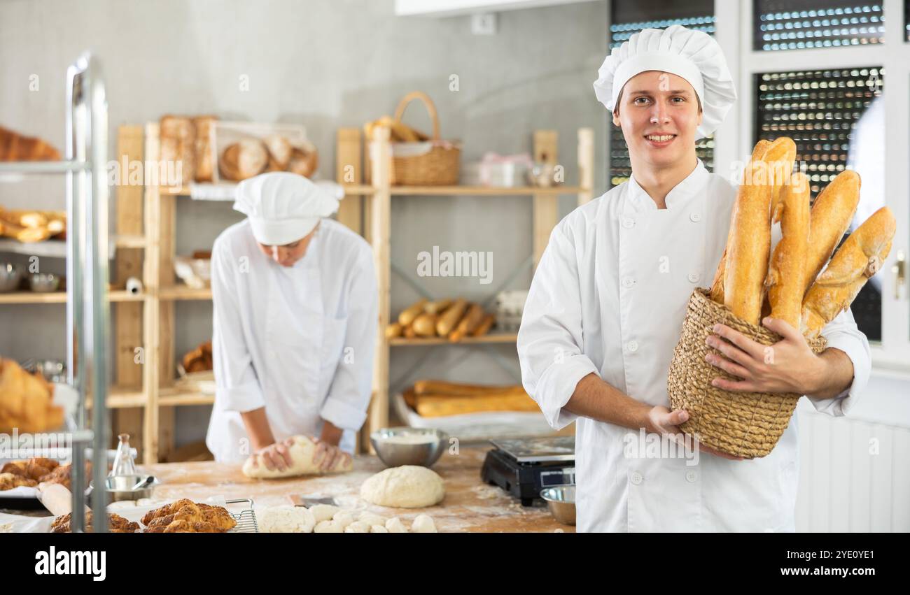 In working room of bakery, there is man with baguettes in wicker basket ...