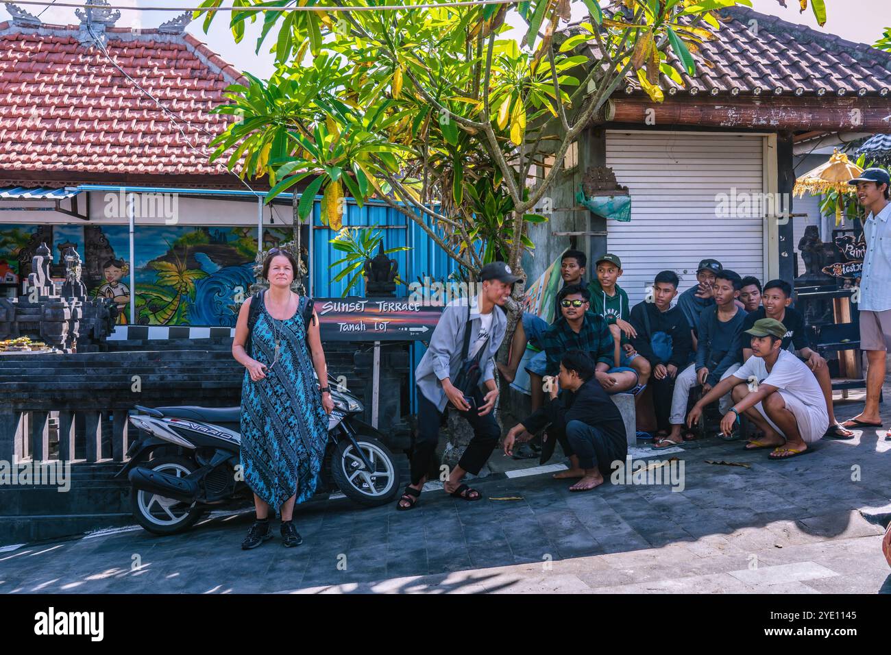 Female tourist walking near a temple in Bali while local young men are ...