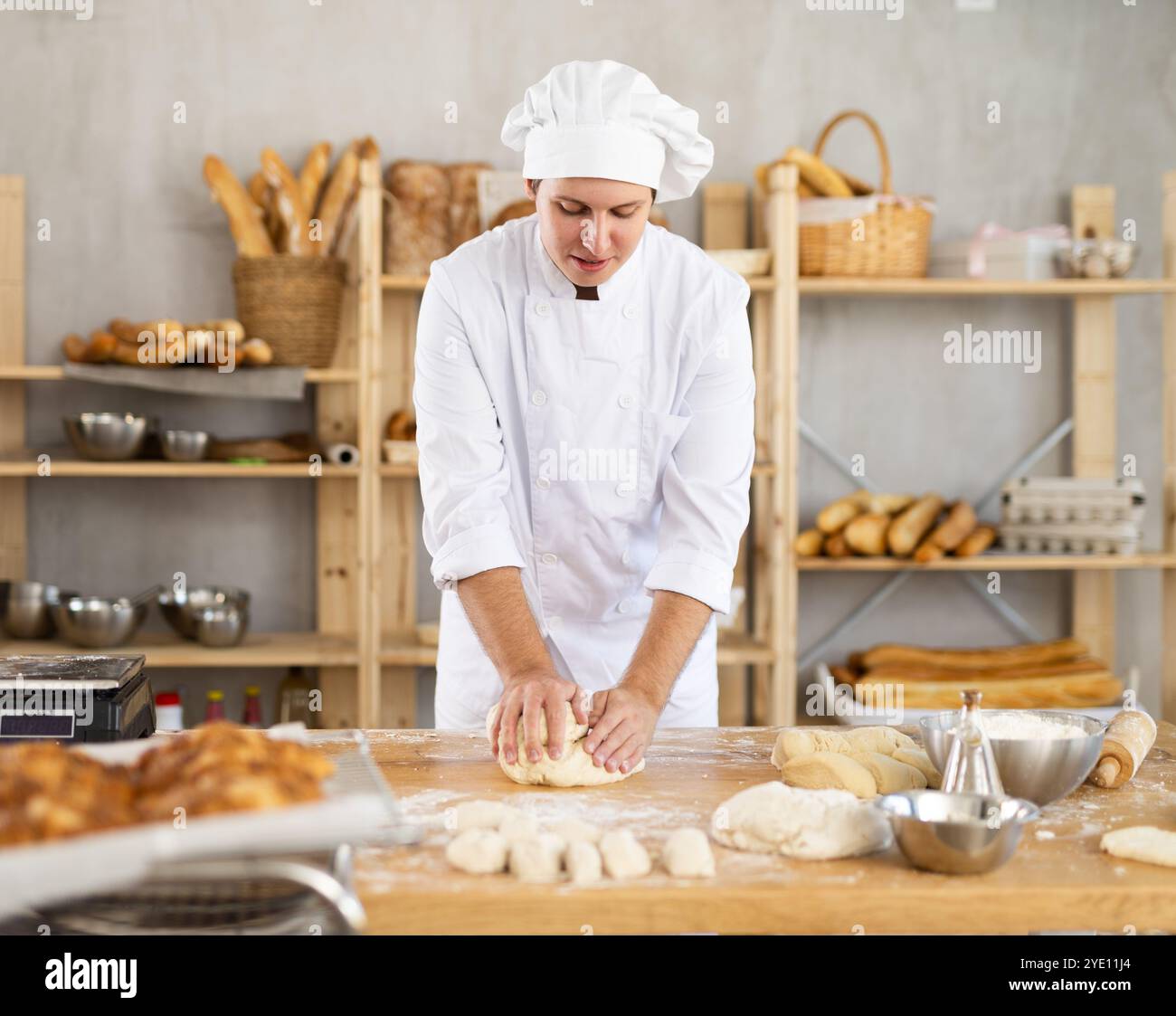 Guy baker in uniform prepares raw dough, kneads it with hands Stock ...