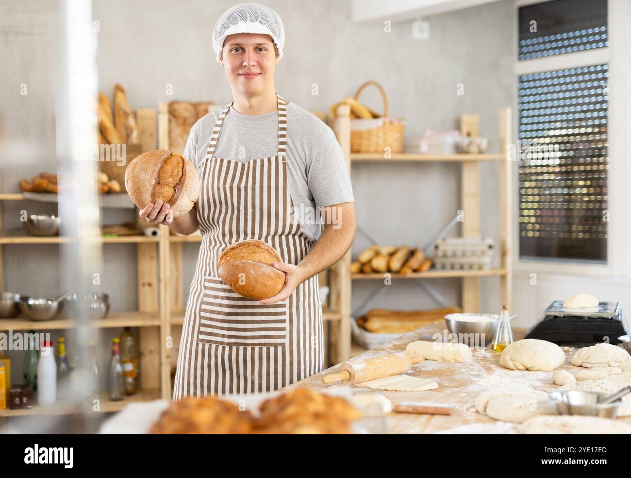 Young man professional baker in apron standing at work table, posing ...