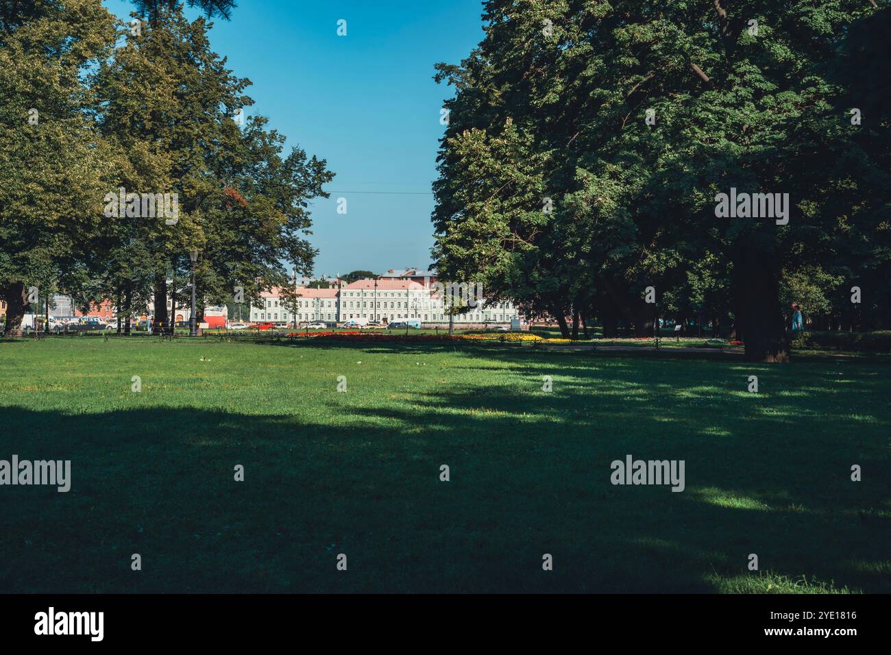 A sunny park scene with large trees and an open green lawn, creating a ...