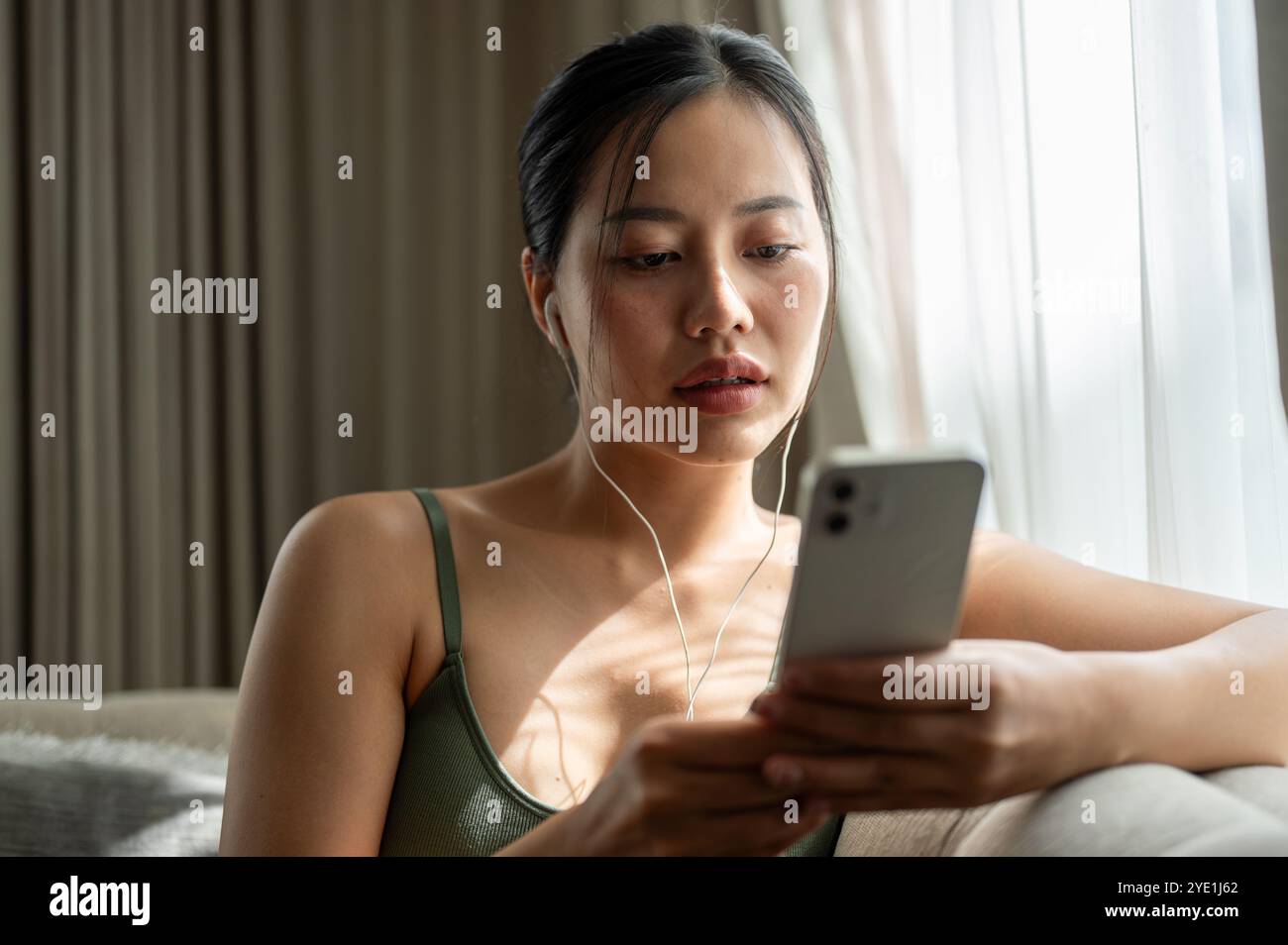 A beautiful Asian woman reading chat on her smartphone while listening to music through her ...