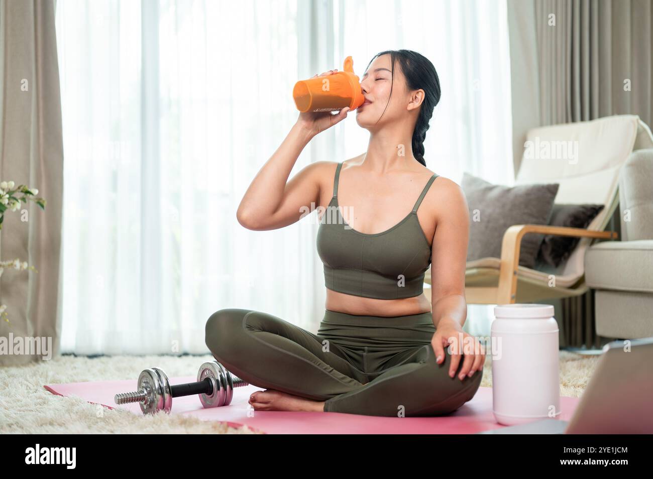 An attractive, slim Asian woman in yoga clothing is enjoying a protein ...