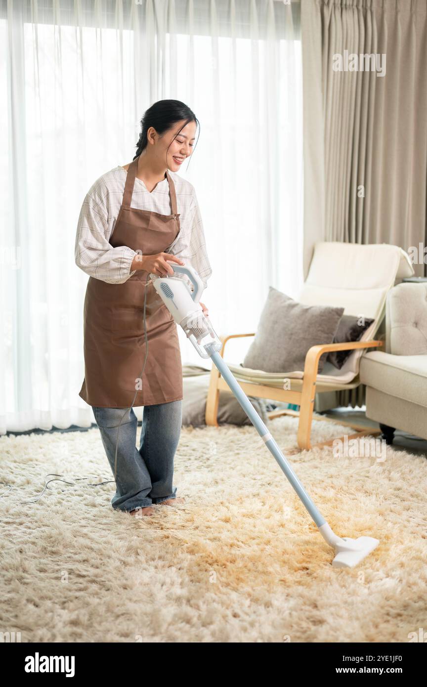 A beautiful Asian woman is cleaning a carpet with a vacuum cleaner in ...