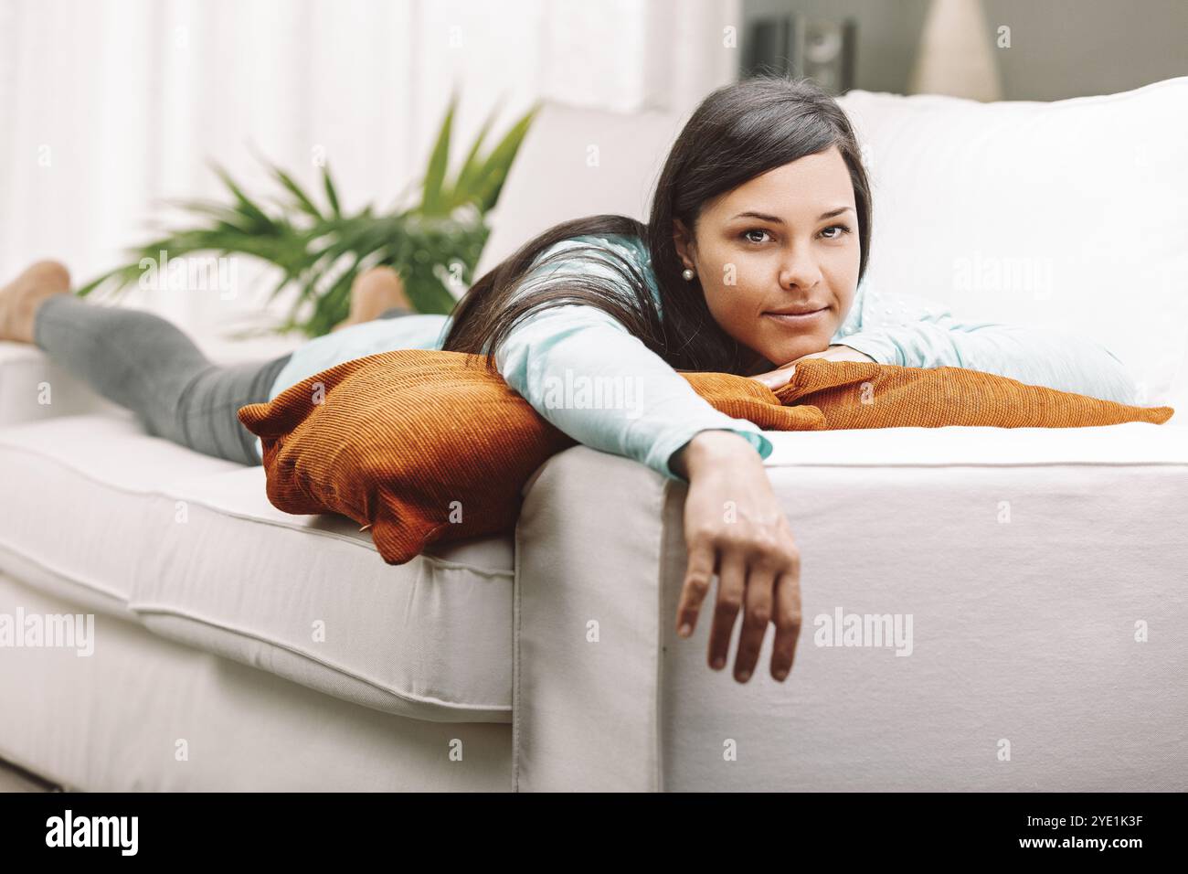 Young woman lies comfortably on a white sofa, her relaxed posture and ...