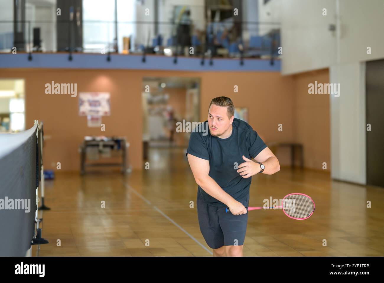 A man is captured mid-action on an indoor badminton court, holding a ...
